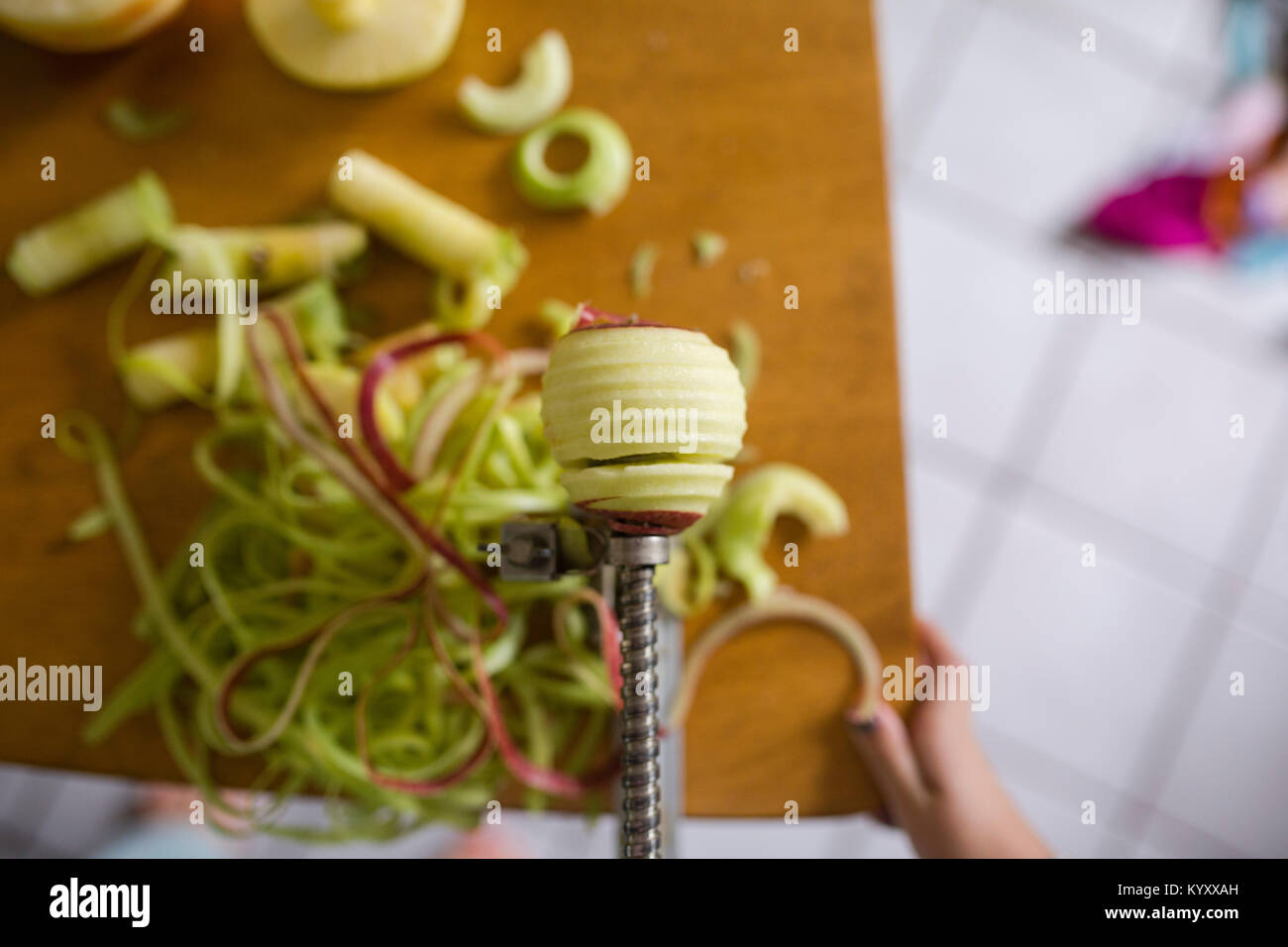 Overhead view of apple being peeled off using peeler on table at home ...
