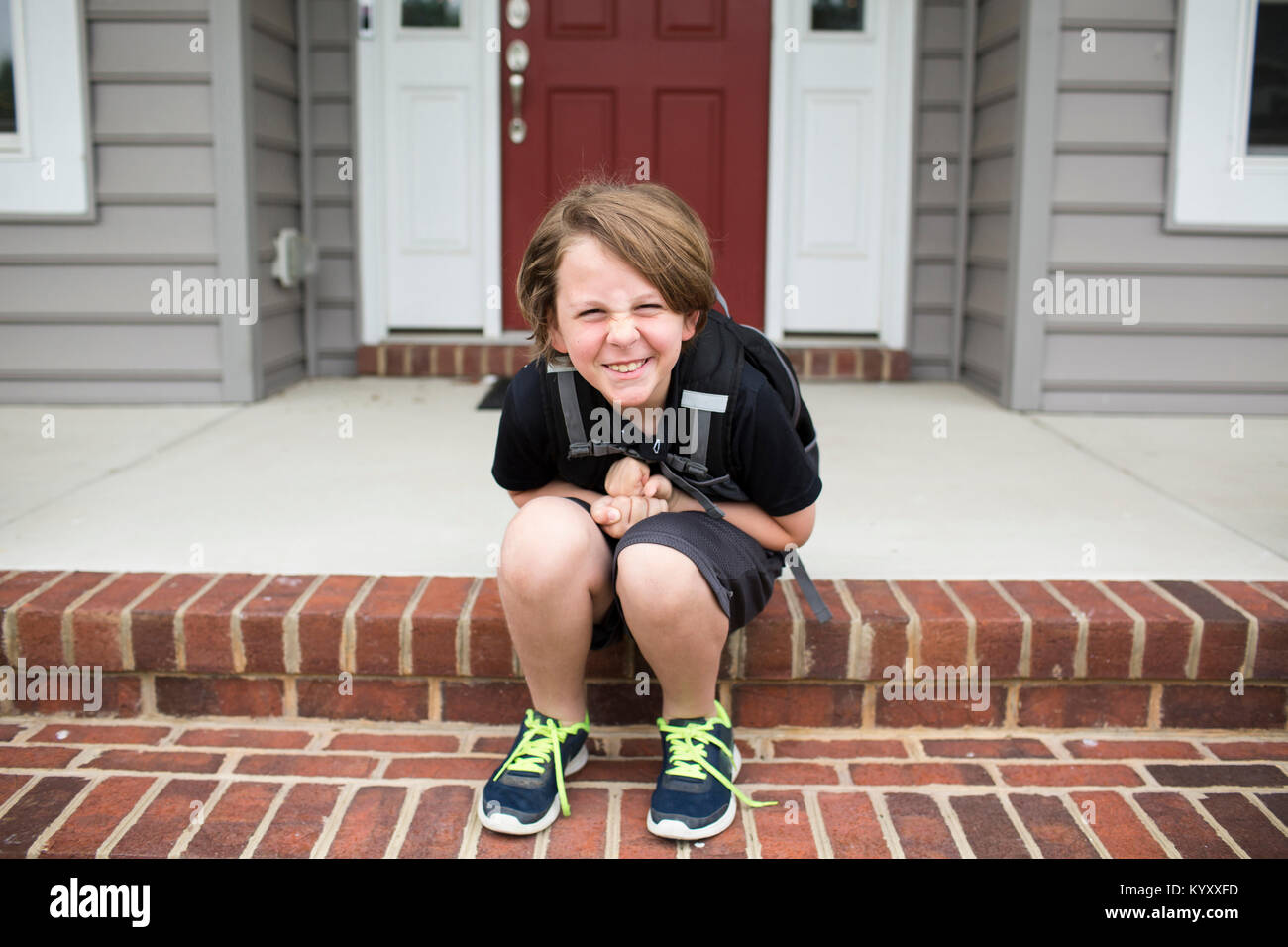 Cheerful boy with backpack sitting on porch Stock Photo - Alamy