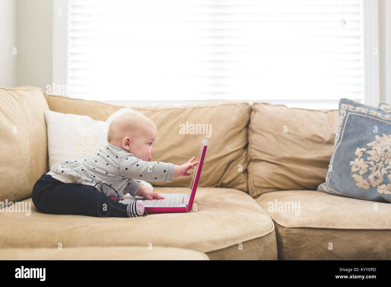 Side view of baby girl playing with laptop computer while sitting on ...