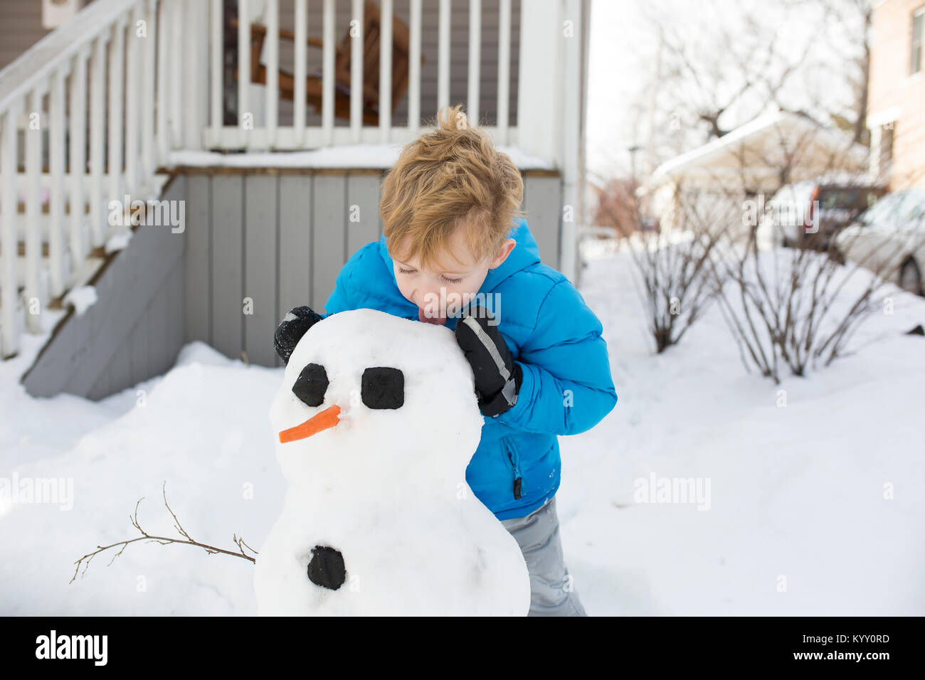 Boy eating snow while making snowman in yard Stock Photo - Alamy