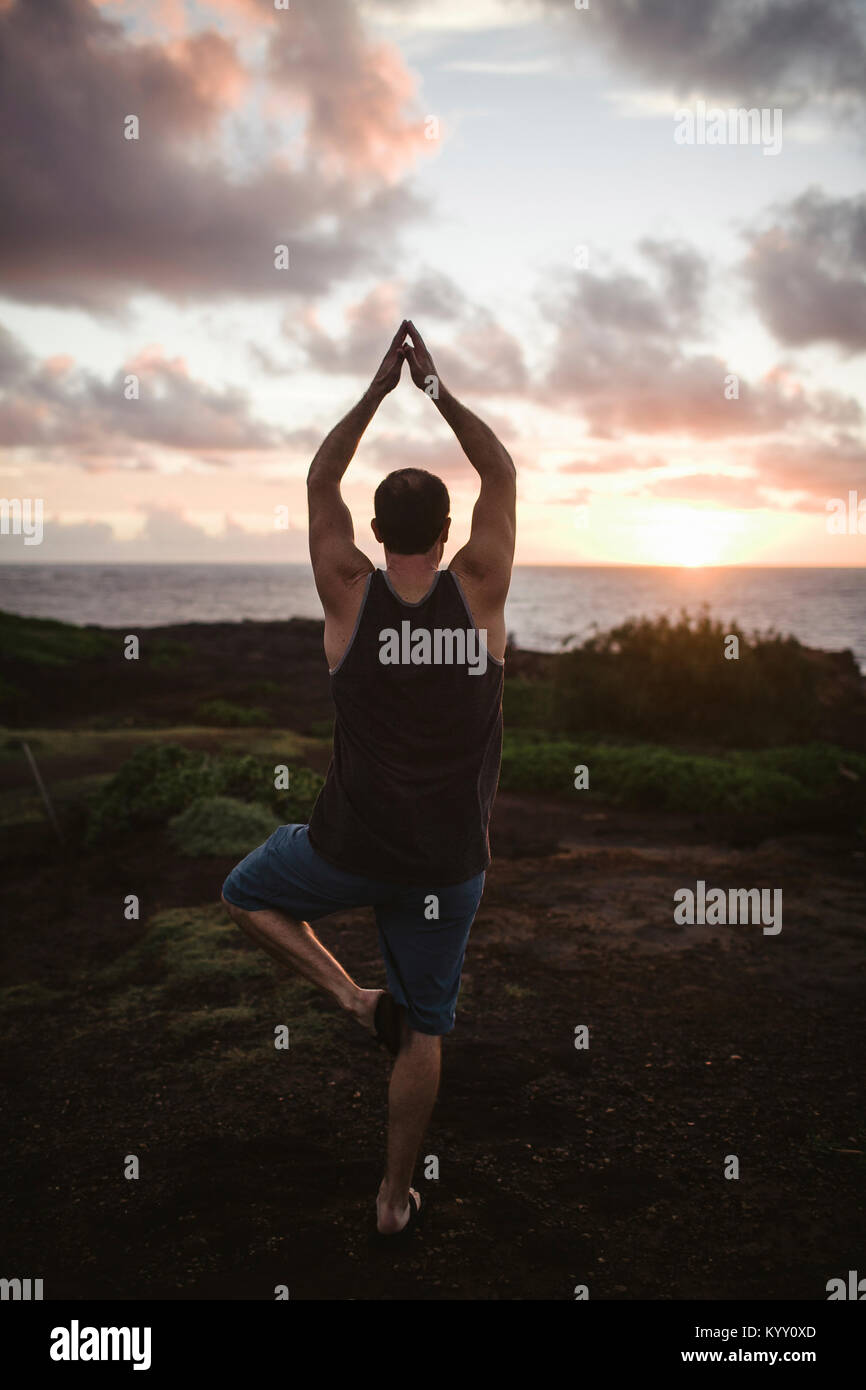 Rear view of man exercising while standing at beach against cloudy sky ...