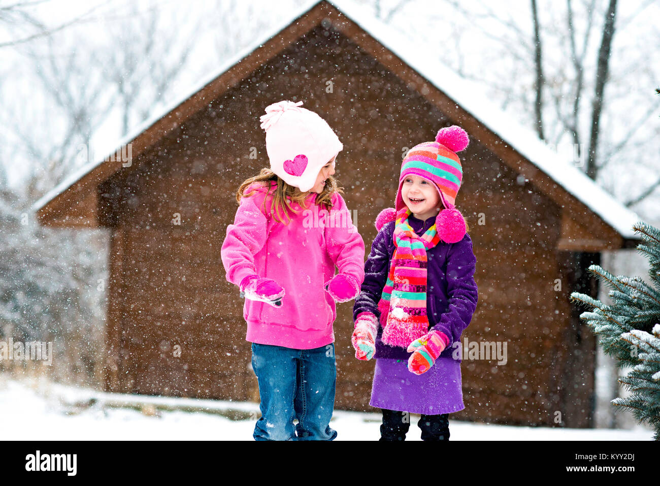 Happy sisters playing with snow while standing outdoors during snowfall ...