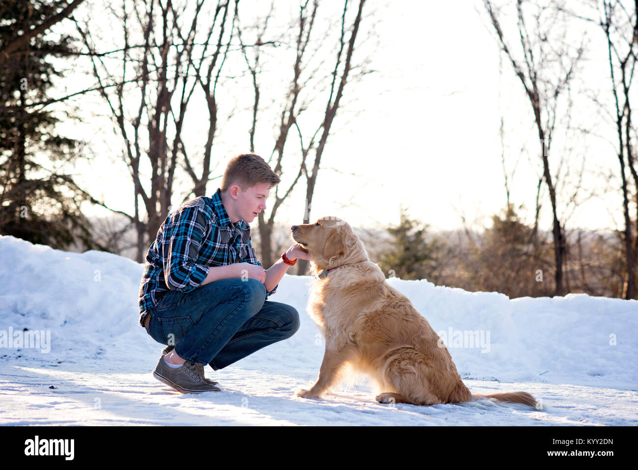 Teenage boy petting dog while crouching on snow covered field Stock ...