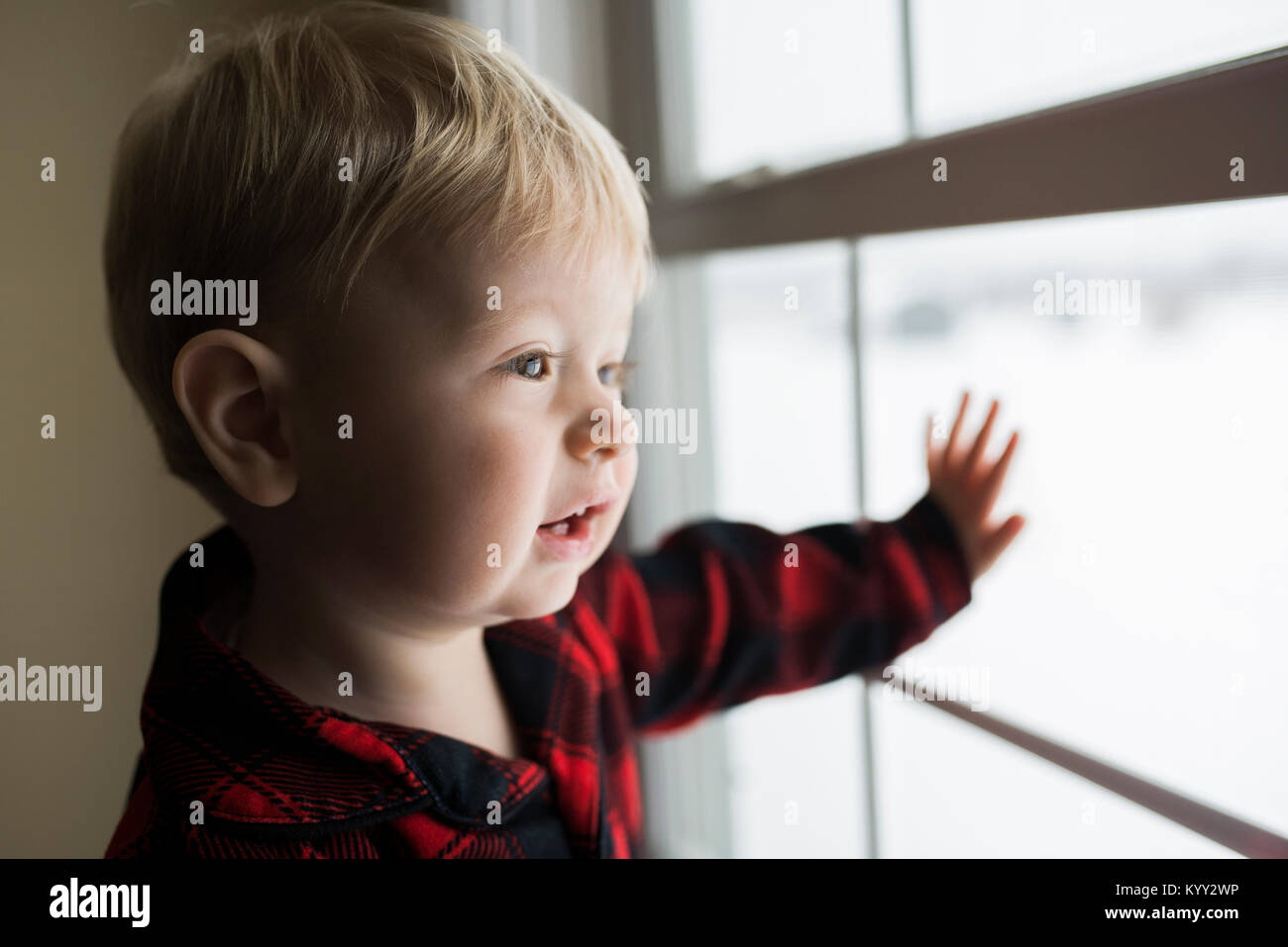 Cute boy looking through window at home Stock Photo - Alamy