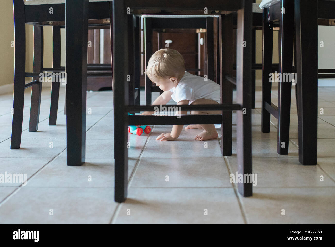 Baby boy playing with toy under dining table at home Stock Photo - Alamy