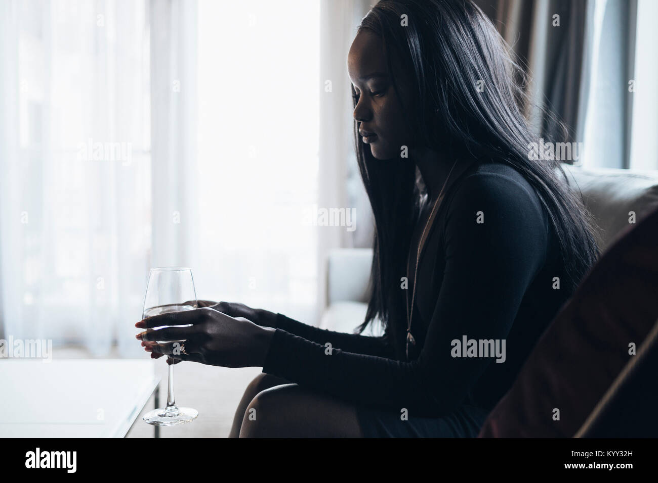 Side view of sad businesswoman holding wineglass while sitting on sofa ...
