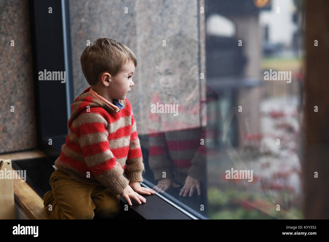 Boy looking through window while kneeling at home Stock Photo - Alamy