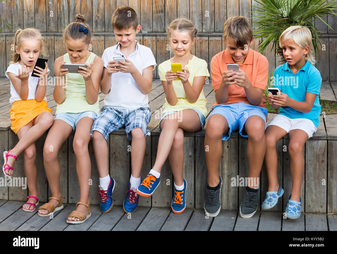 cheerful european children in school age looking at mobile phones and ...