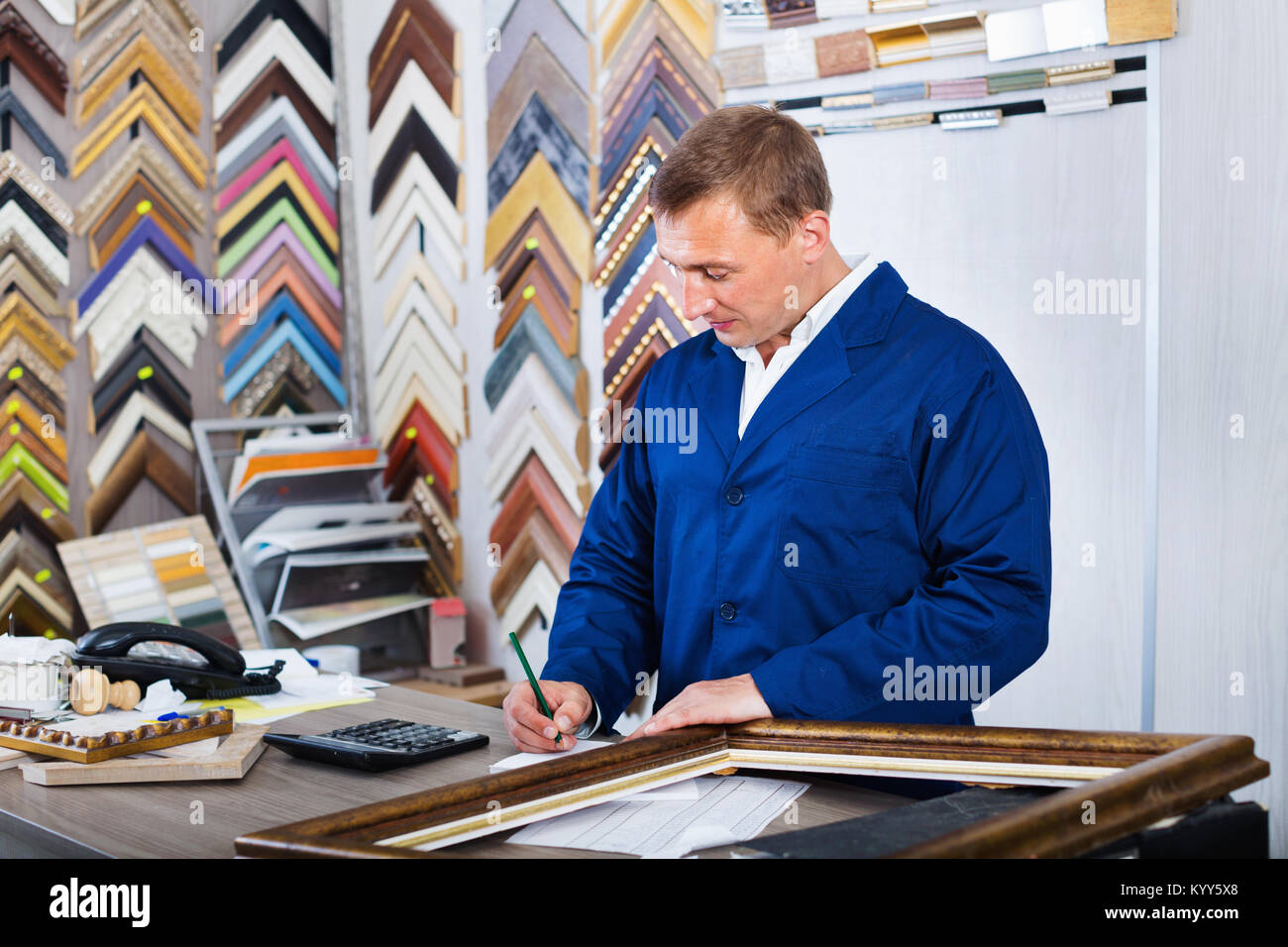 Cheerful diligent man worker holding picture frame details on counter ...