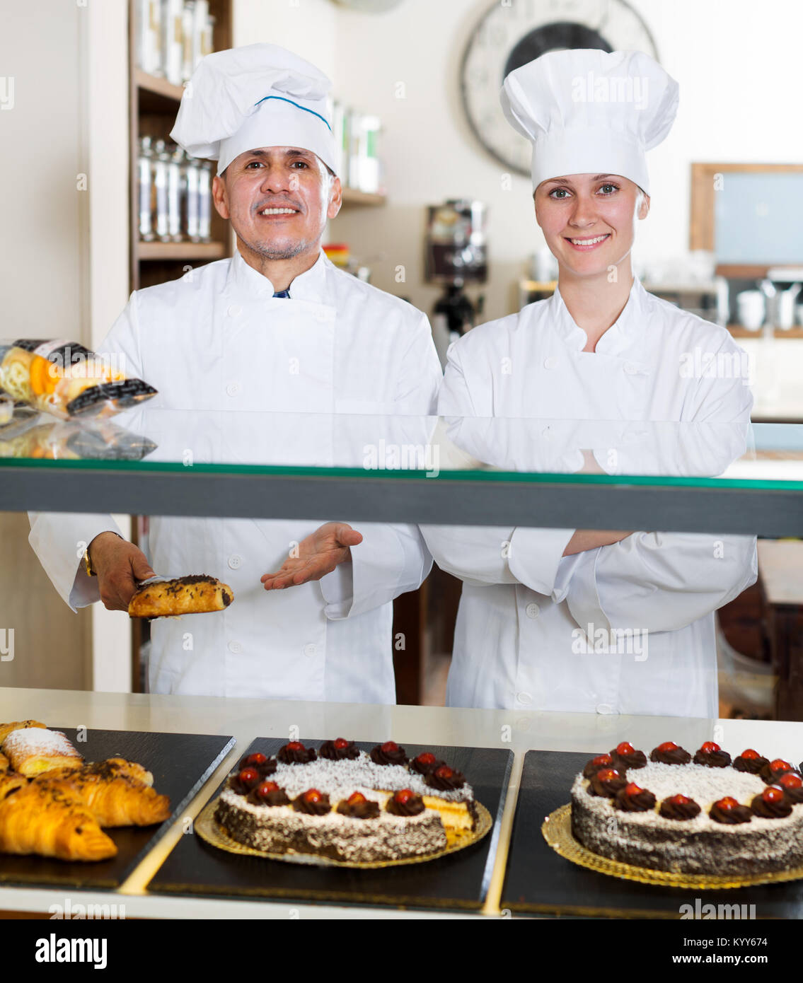 Cheerful experienced man and woman staff offering cakes and buns in ...
