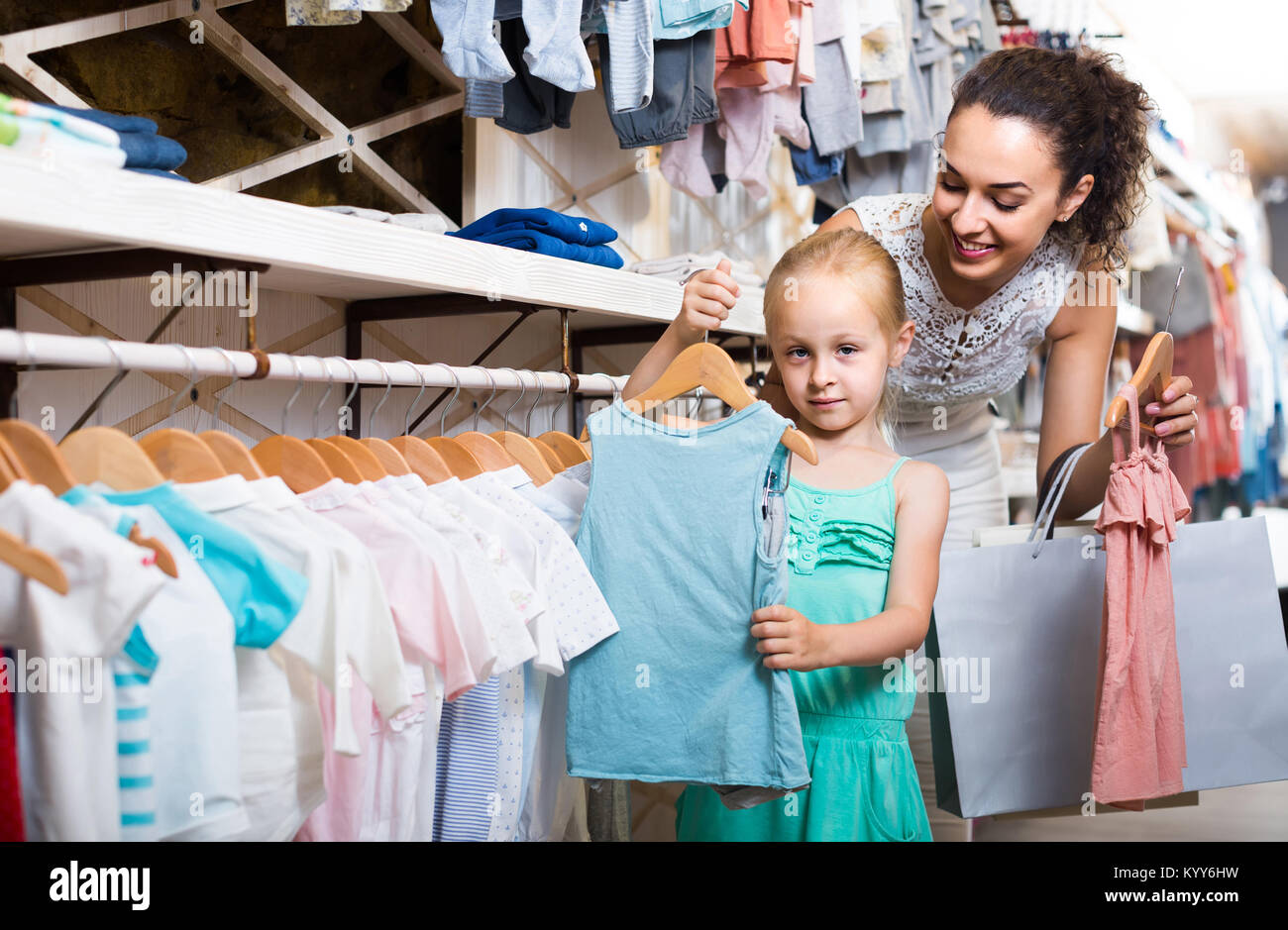 portrait of positive woman and girl shopping kids apparel in clothes ...
