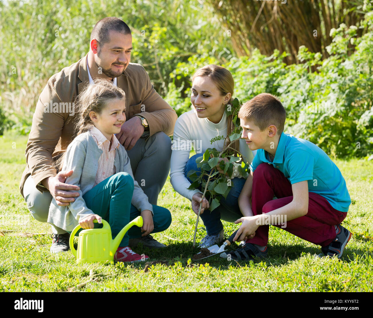 Cheerful young parents with two smiling children planting a tree ...