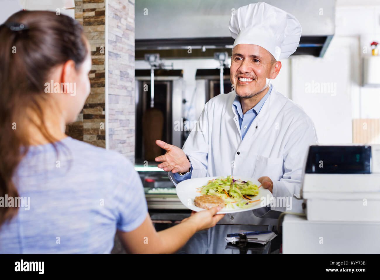 Mature positive man chef wearing uniform giving kebab plate to customer ...