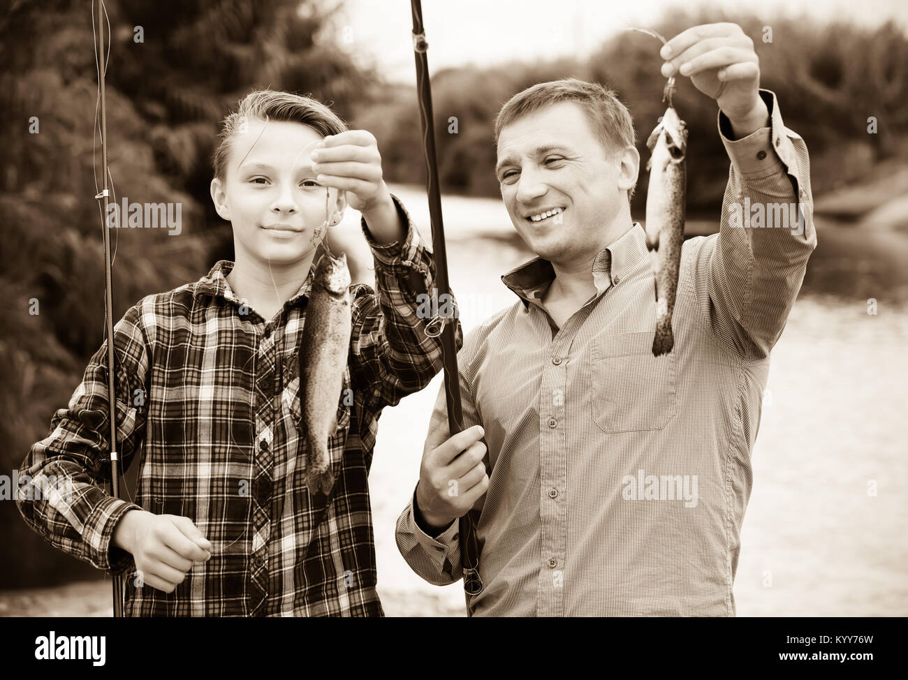 Positive teenage boy and his father holding fish on hook in hands Stock ...
