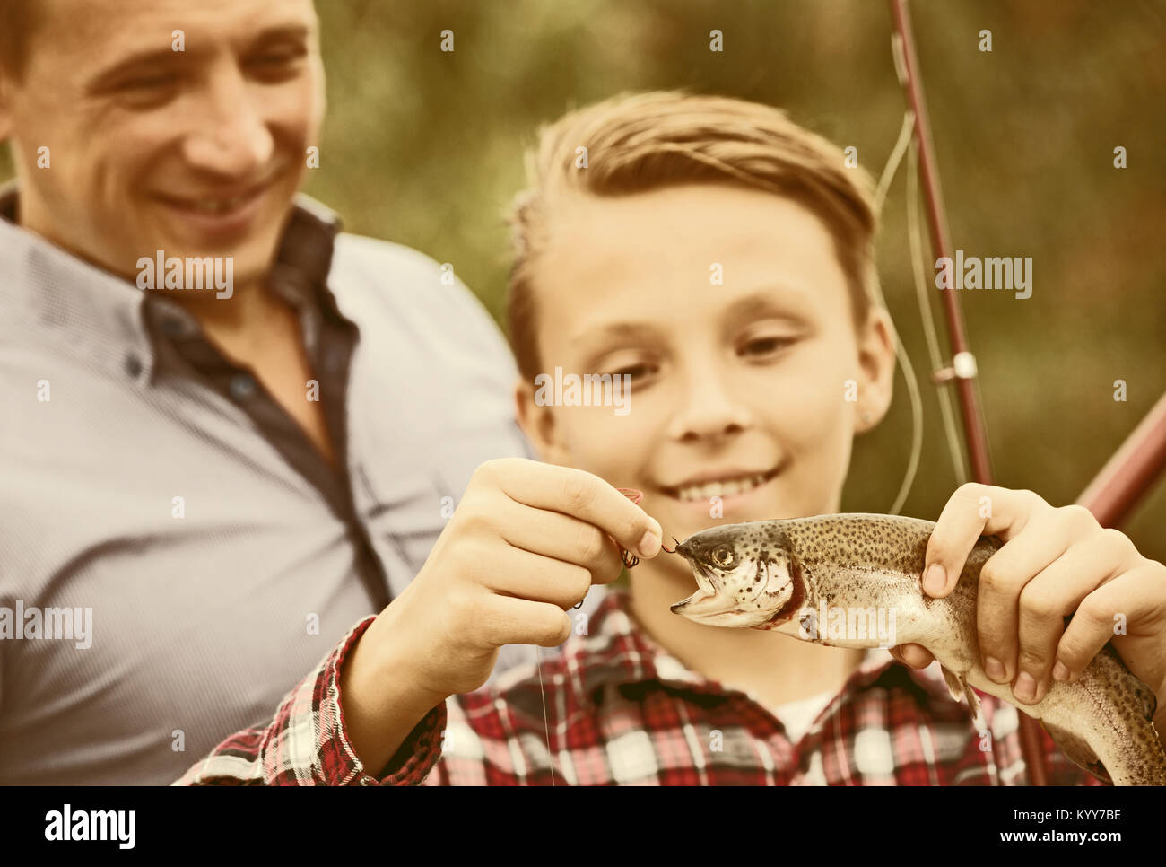 Happy man with teenager boy releasing fish from hook outdoors. Focus on ...