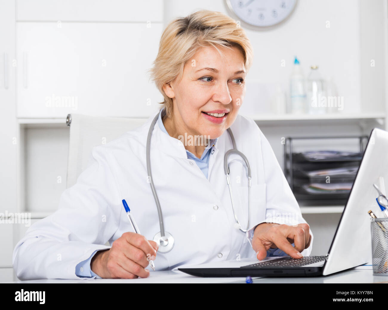 Mature doctor in white medical dressing gown waiting patients visit ...