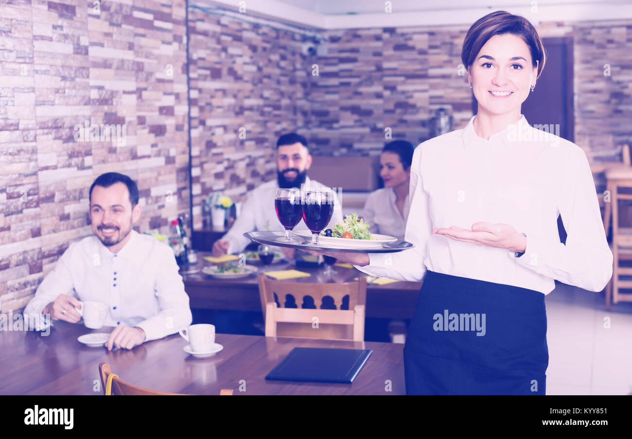Positive young waitress greeting customers at table in restaurant Stock ...