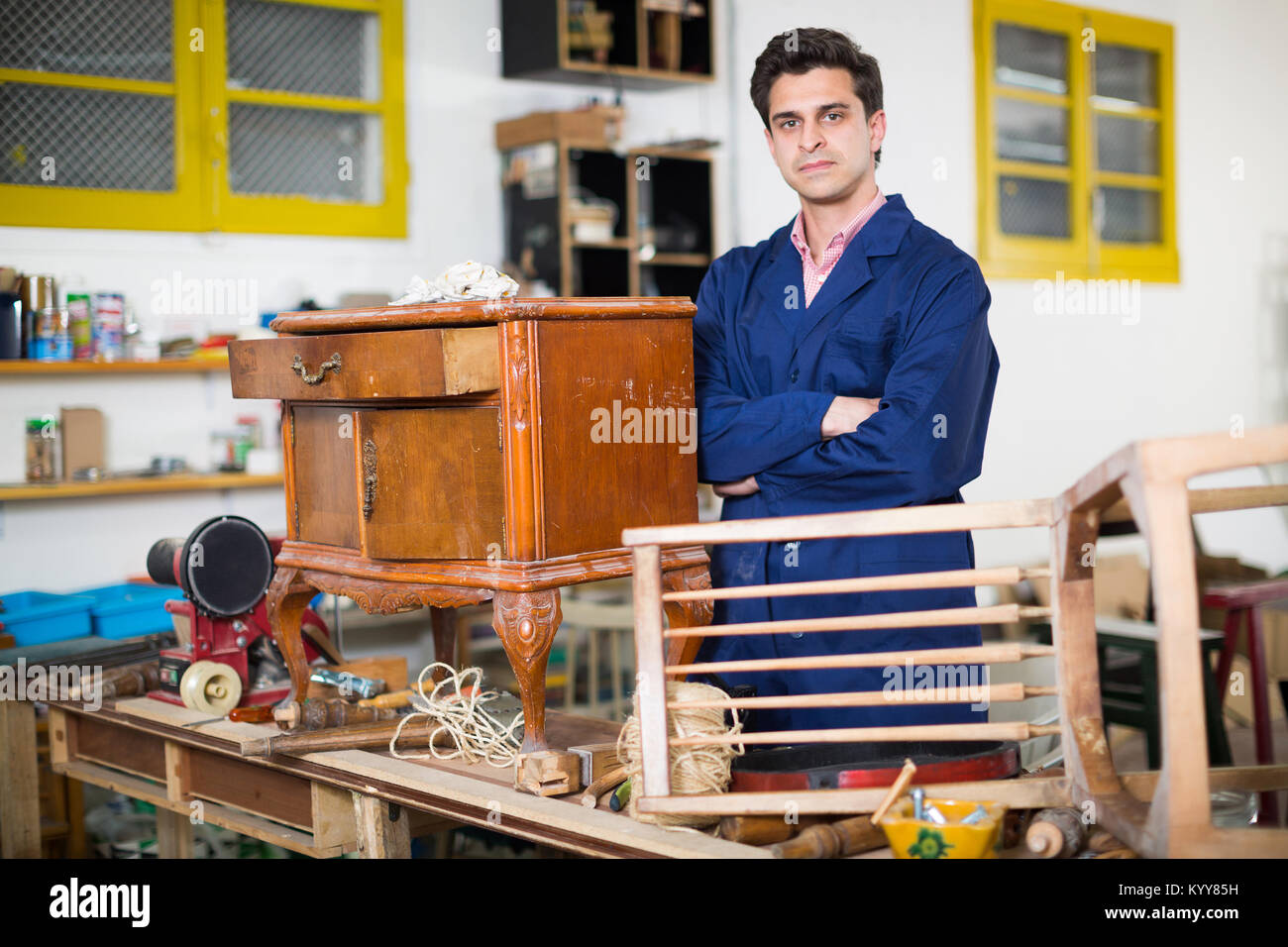 Man carpenter wearing blue overalls restoring furniture in restoration ...