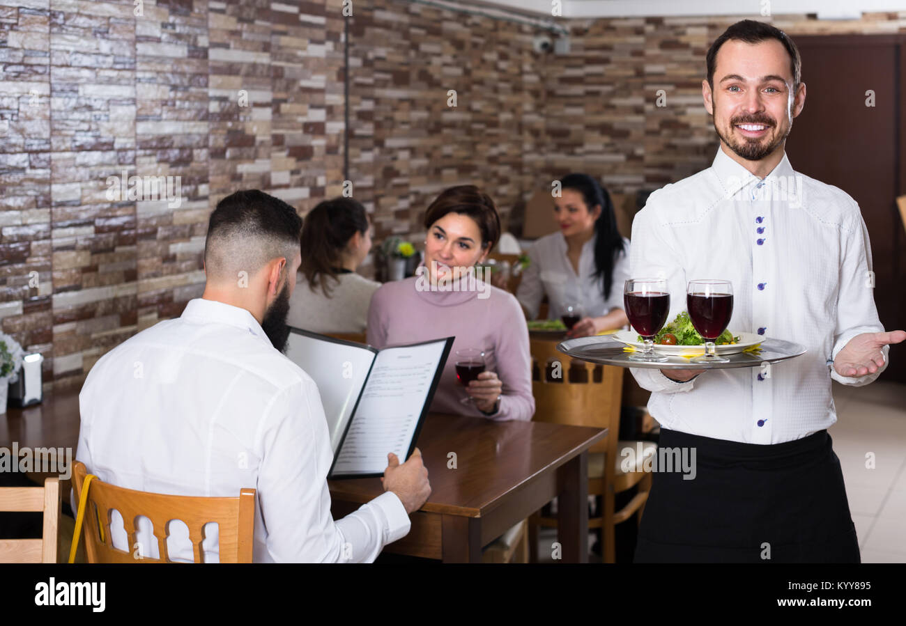 Portrait of adults guest in middle class restaurant and happy waiter ...
