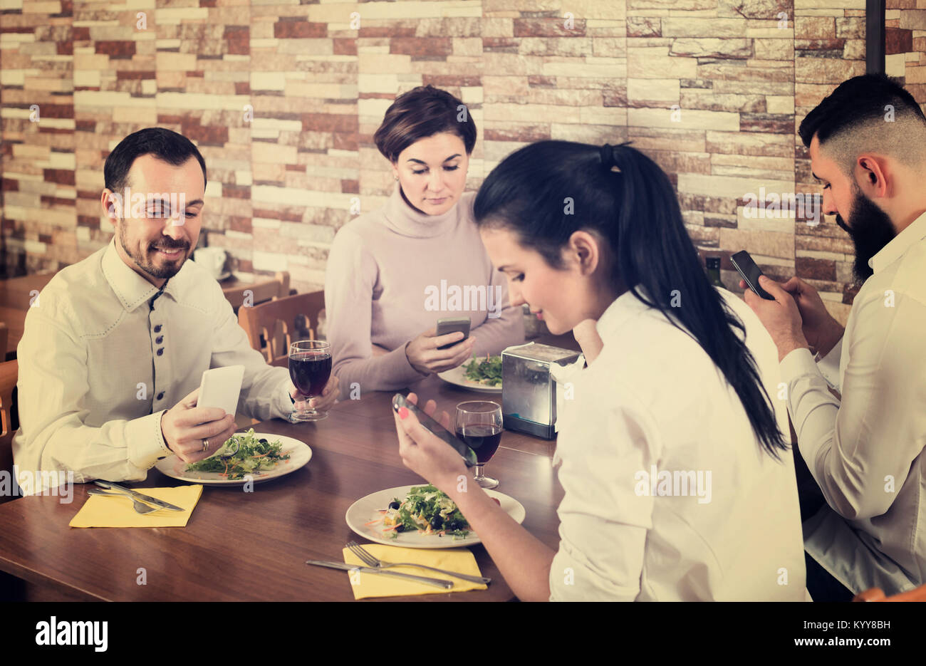 group of young friends busy with phone ignoring dinner in restaurant ...