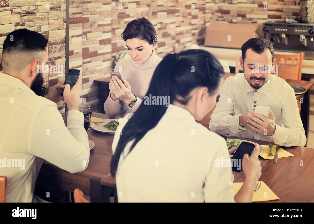 group of cheerful friends busy with phone ignoring dinner in restaurant ...
