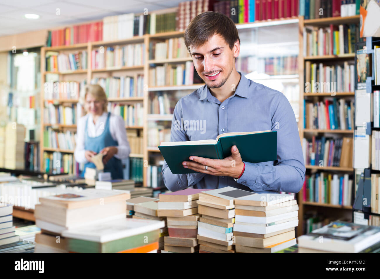 portrait of man looking at open book standing among bookshelves Stock ...