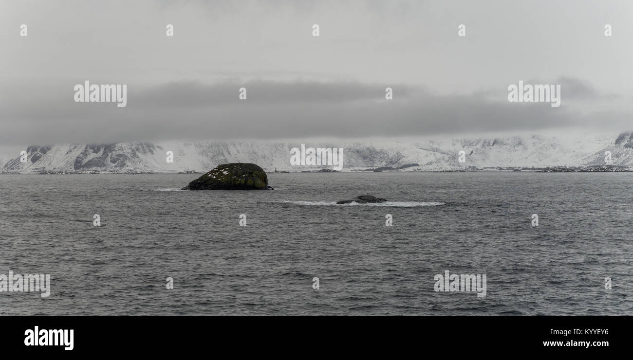 Rock formations in sea with mountain range in the background, Lofoten ...
