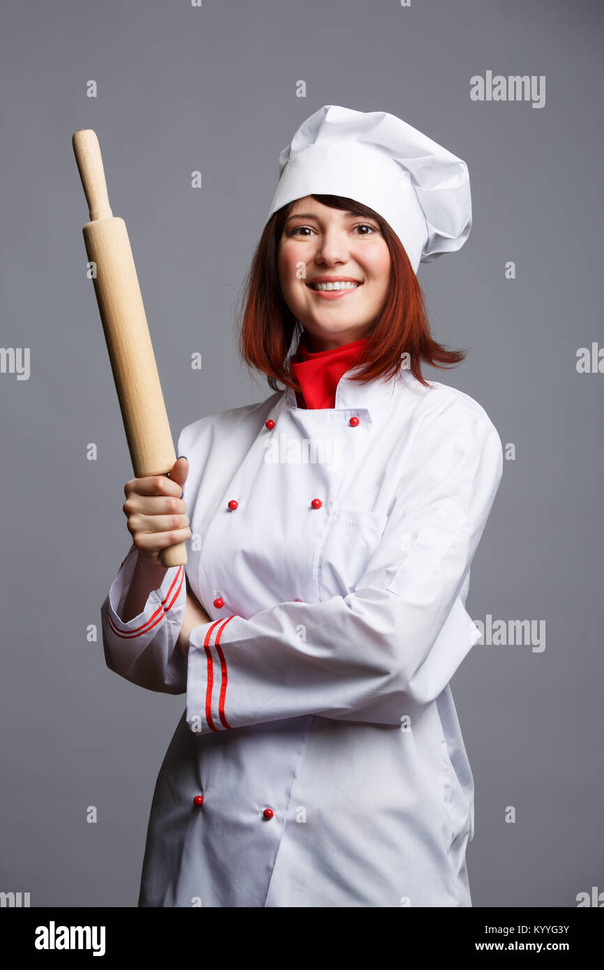 Image of brunette cook in white coat and cap with rolling pin in hands ...