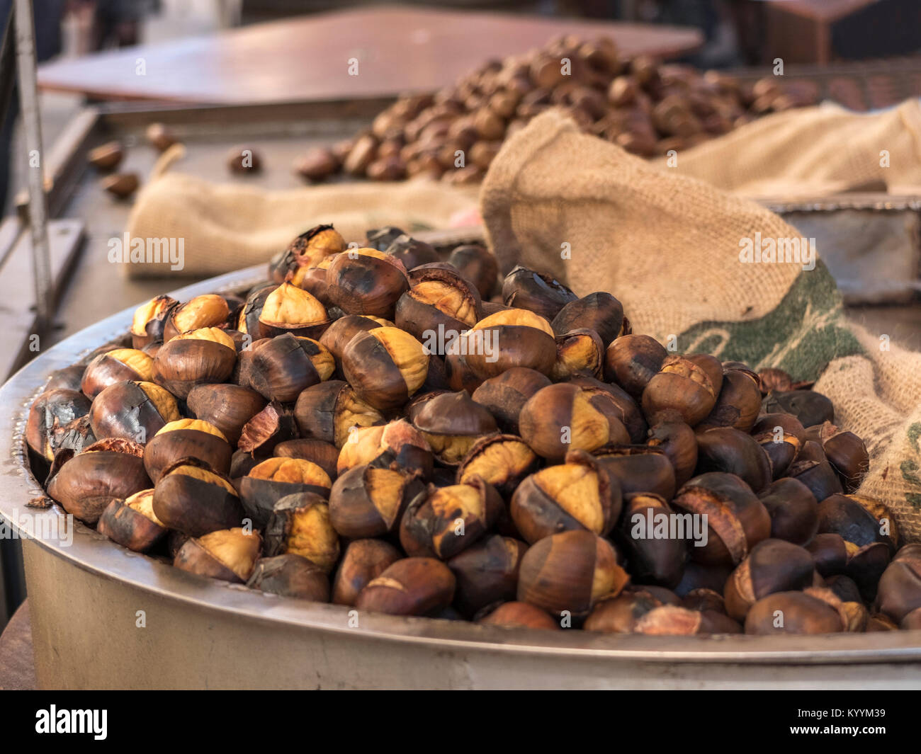 Roasted chestnuts cooked on a bin with wood fire. Near jute bags for ...