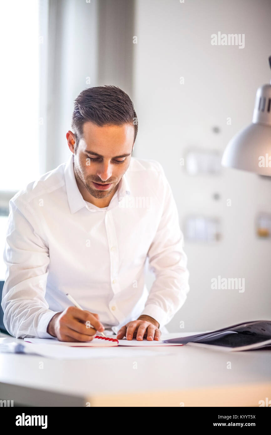Young businessman writing notes at desk in office Stock Photo - Alamy