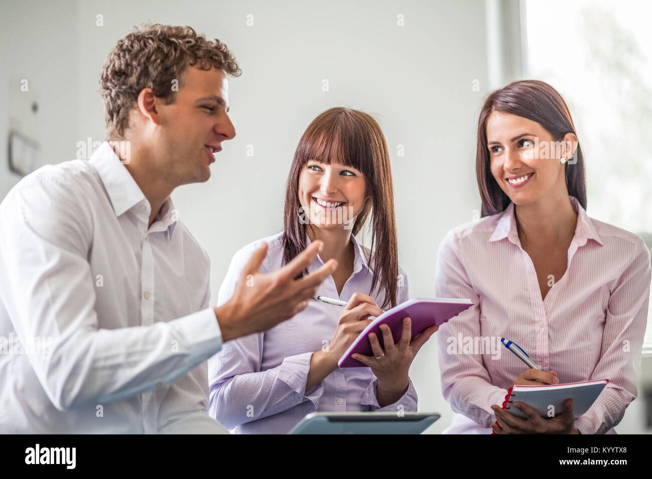 Young businessman explaining while female colleagues writing in books ...