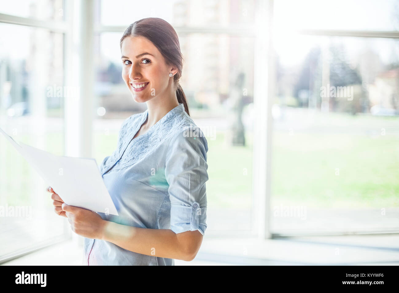 Portrait of happy young businesswoman holding documents in office Stock ...