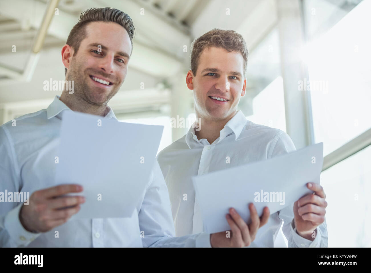 Portrait of happy young businessmen reviewing documents in office Stock ...