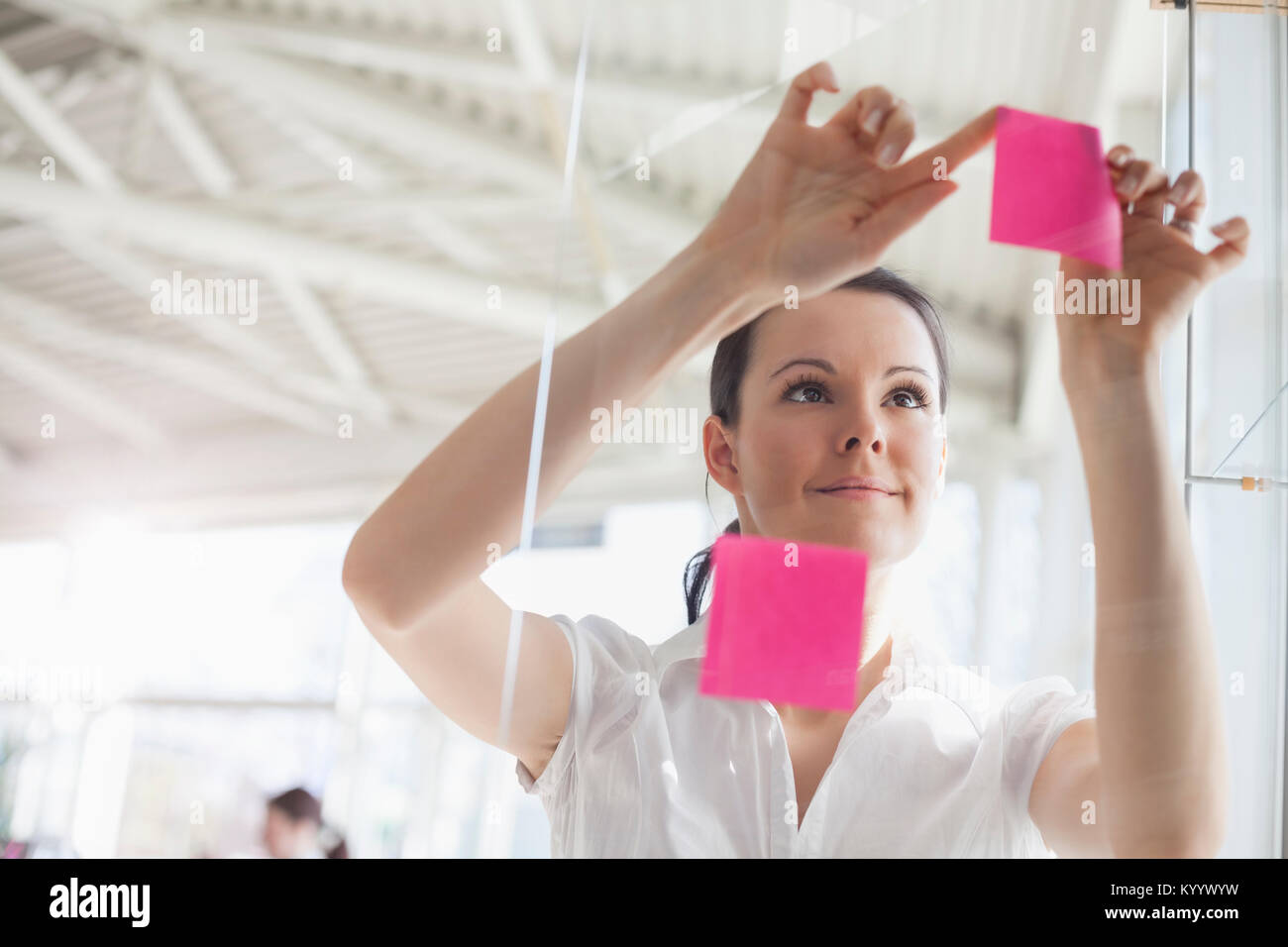 Beautiful young businesswoman putting sticky notes on glass wall in ...