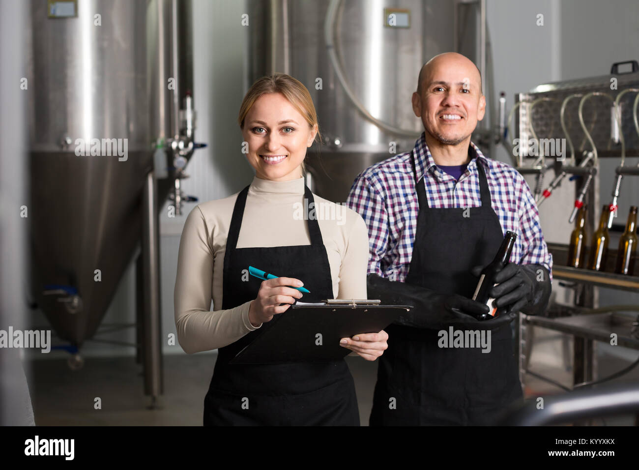 Portrait of two positive smiling workers on beer brewery factory. Focus ...