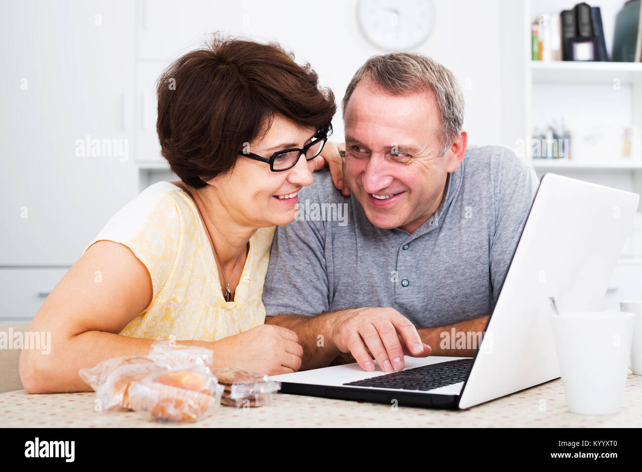 Happy senior man and woman sitting and using computer together at home ...
