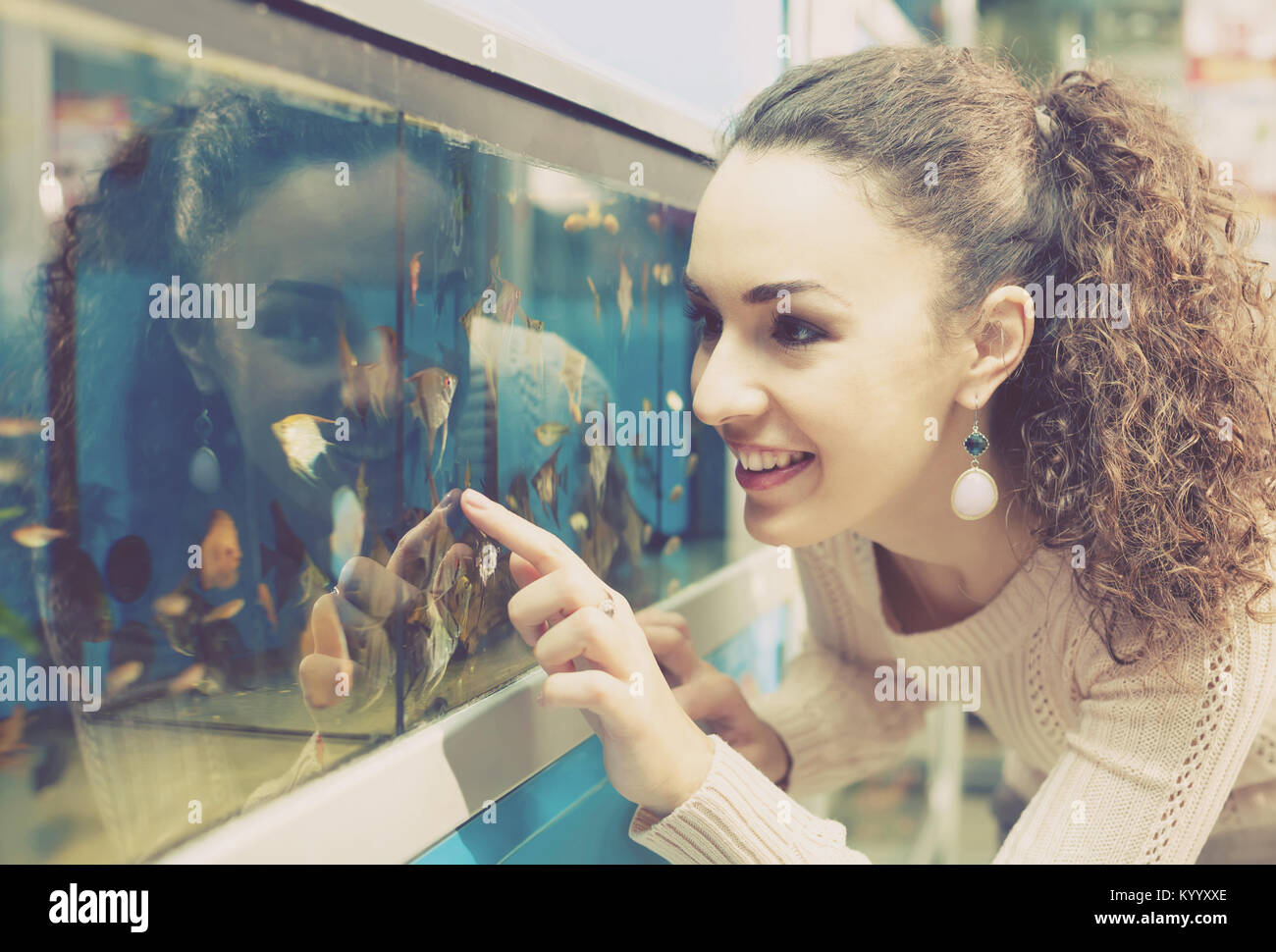 smiling russian female customer watching tropical fish in aquarium tank ...