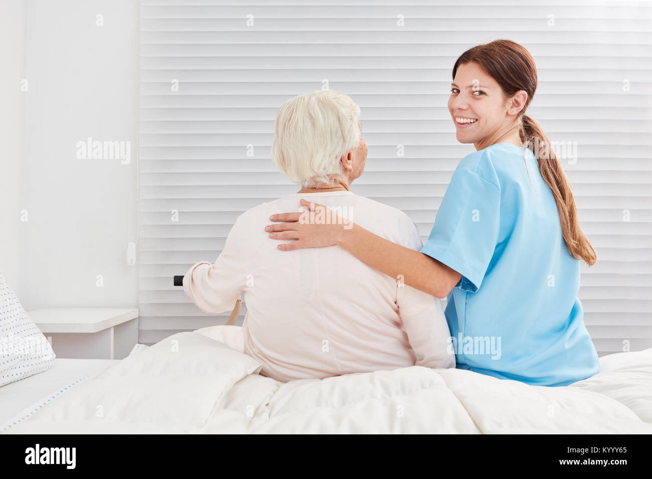 Young woman as nursing assistant or nurse helps senior woman out of bed ...