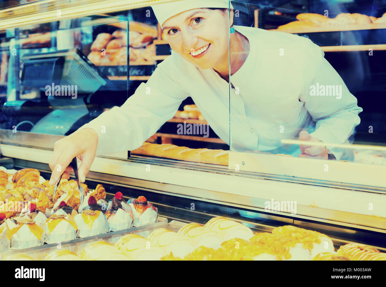 friendly smiling mature female baker offering fresh pastry at the ...