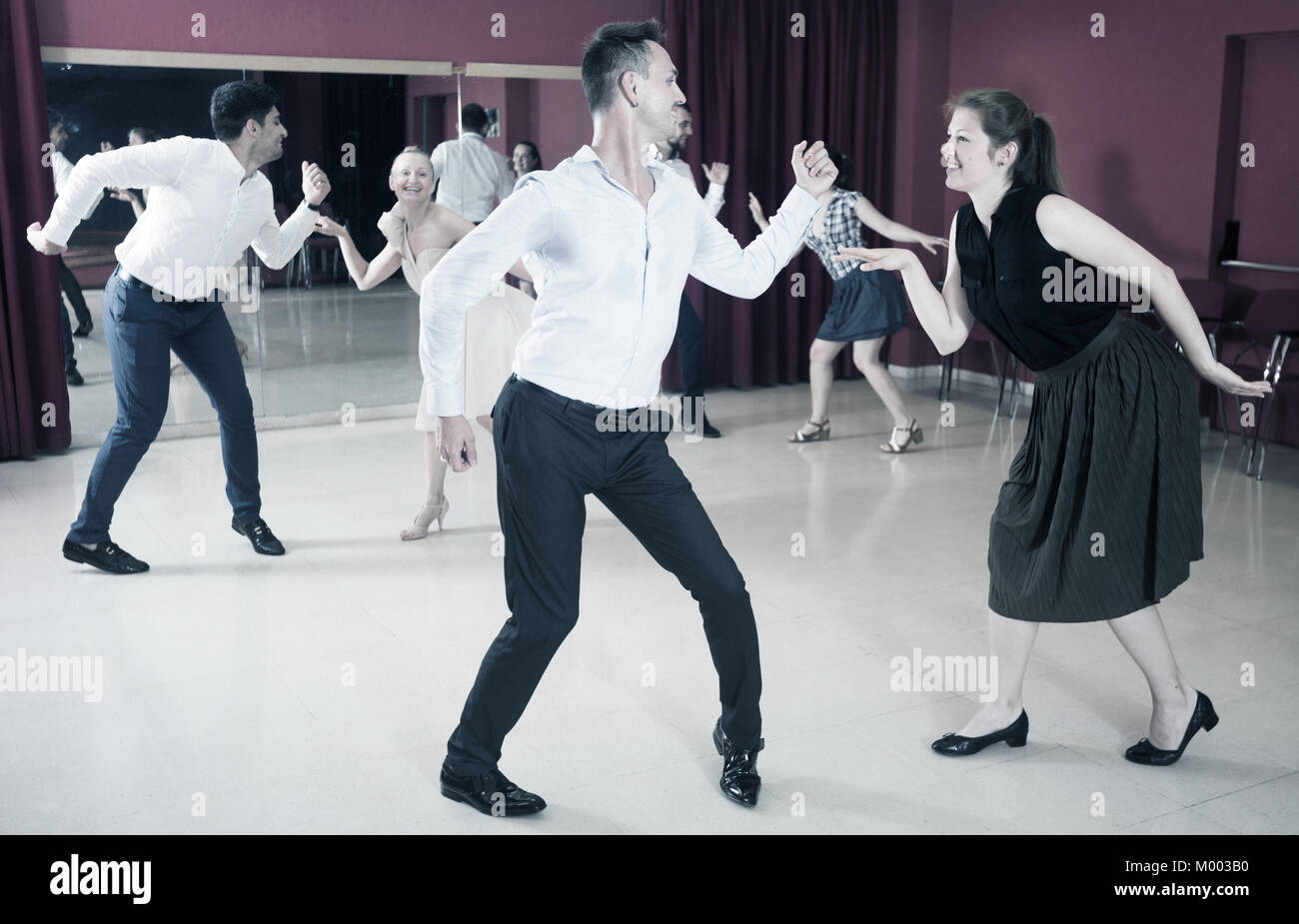 Young smiling people practicing vigorous twist movements in dance class ...