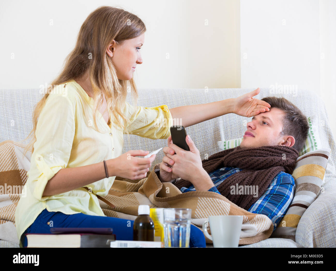 Young wife taking care of sick husband lying on sofa under blanket ...