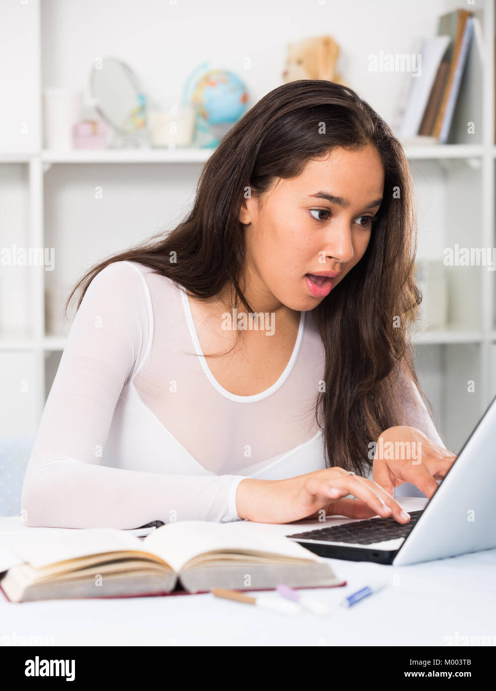 Young girl reading info in laptop and surprised indoors Stock Photo - Alamy
