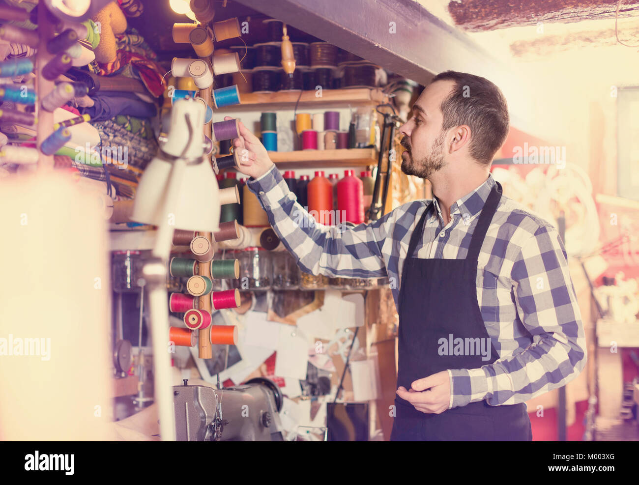 Young man worker examining threads for sewing in leather workshop Stock ...