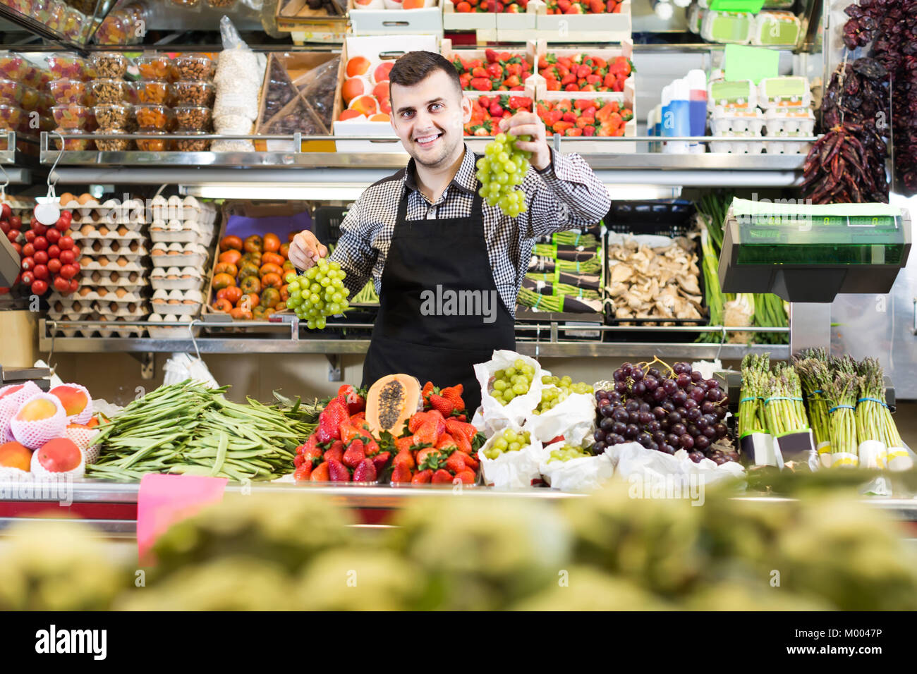 happy russian male shopping assistant weighing grapes in grocery shop ...