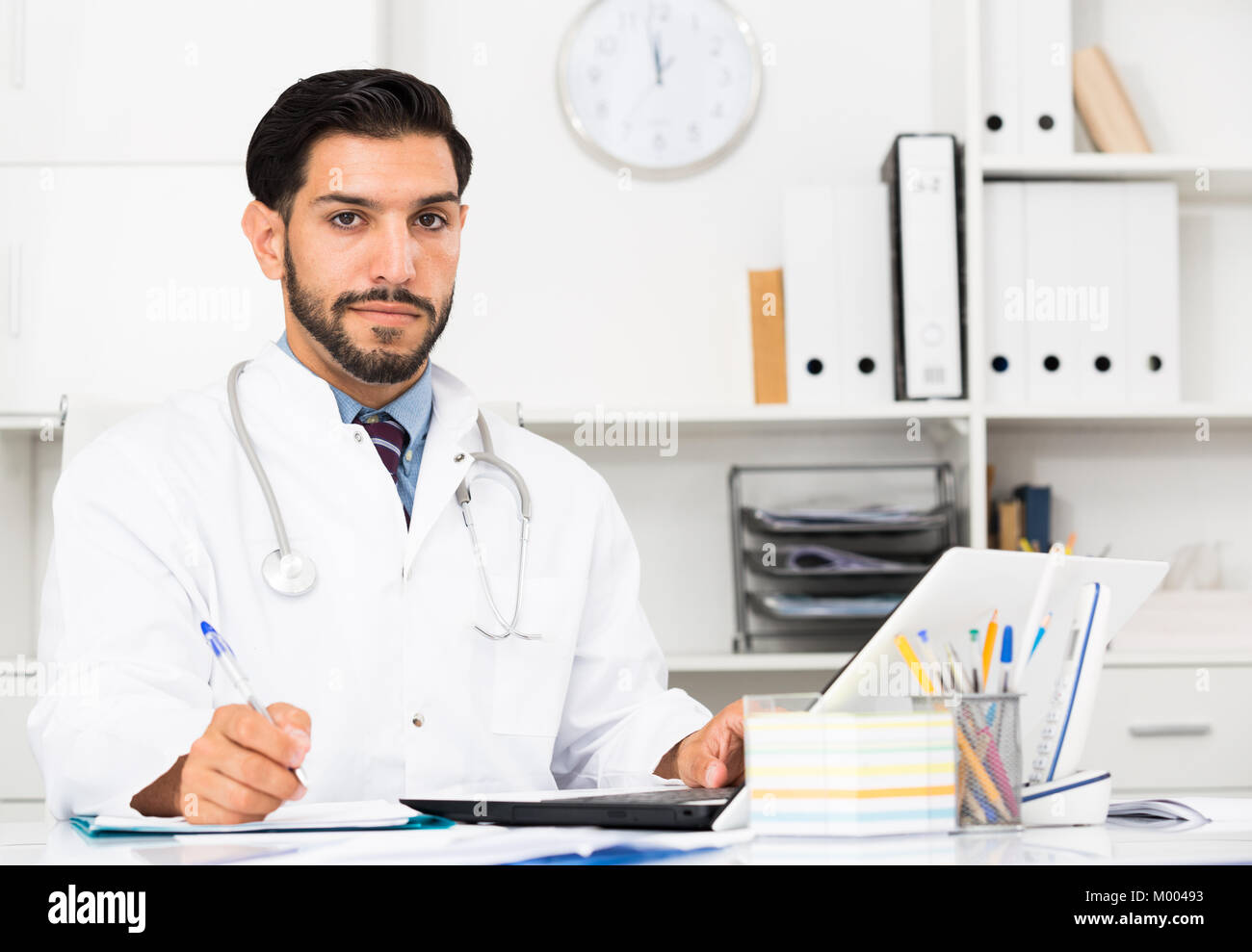 Spanish man doctor is working with documents behind laptop in his ...