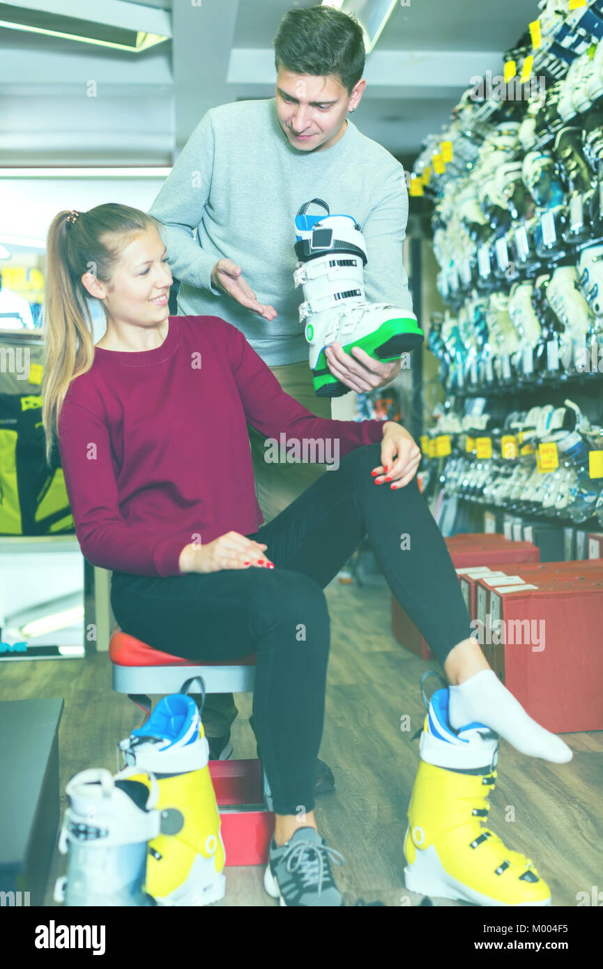 Salesman is helping woman to trying on boots for skiing in sport store ...