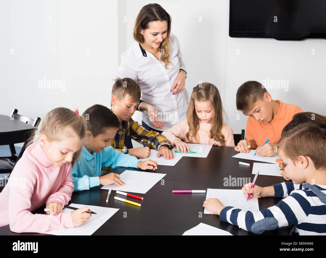 Professor and elementary age children drawing at classroom in school ...