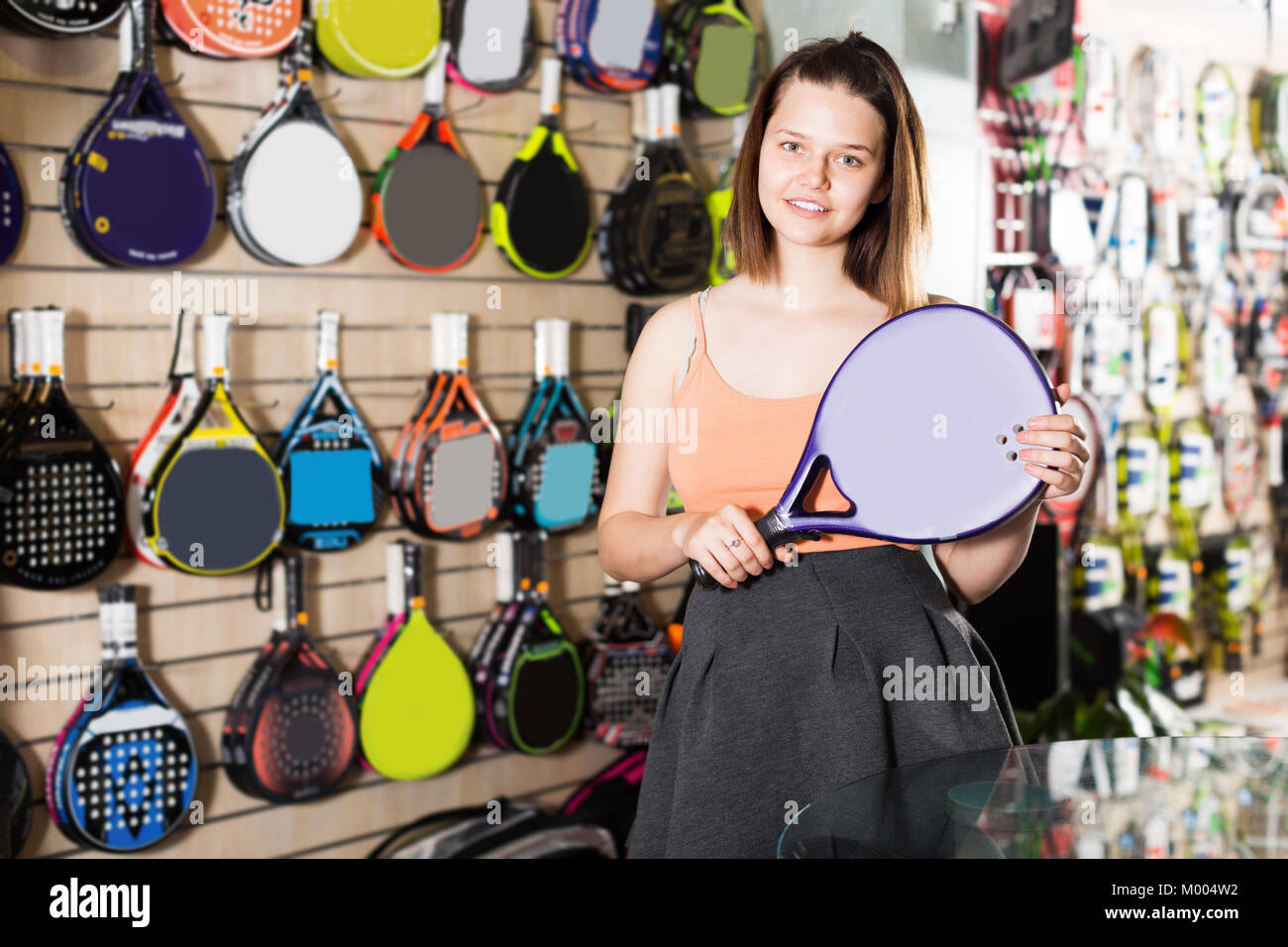 Smiling teen girl holding in hand racket for squash in sport store ...