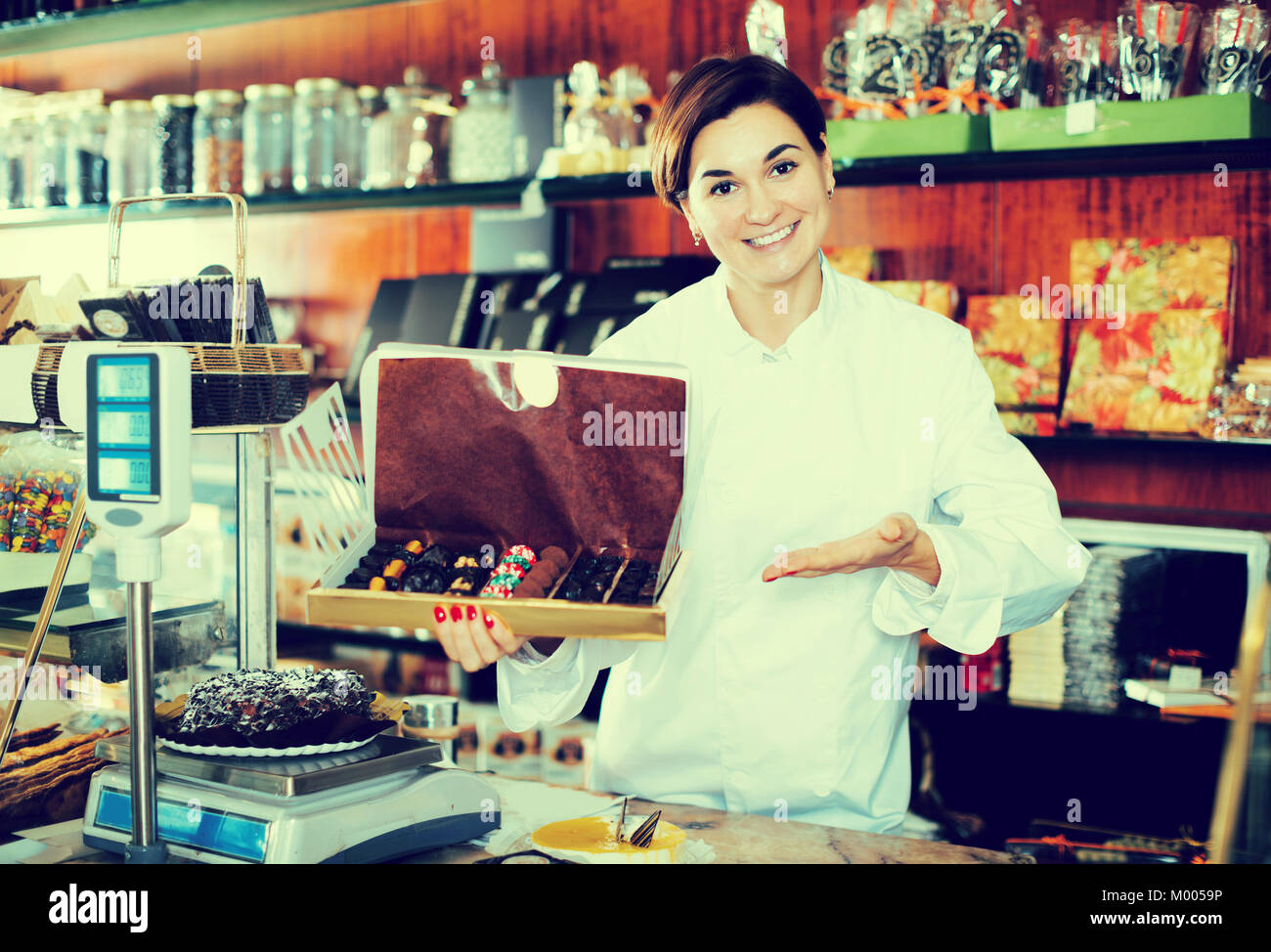 Smiling young shop assistant demonstrating box of delicious chocolates ...