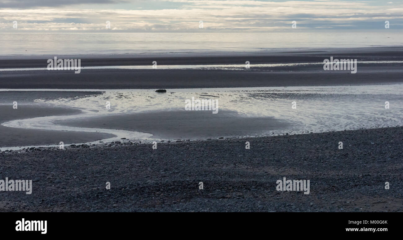 An extremely low tide exposues a large expanse of a grey gravel and ...
